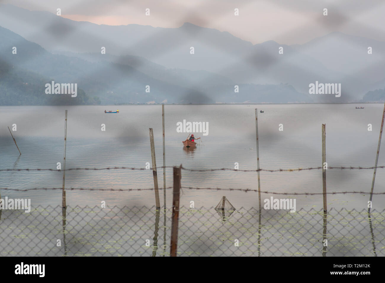 A fisherwoman on a boat on Phewa lake in Pokhara through a chainlink ...