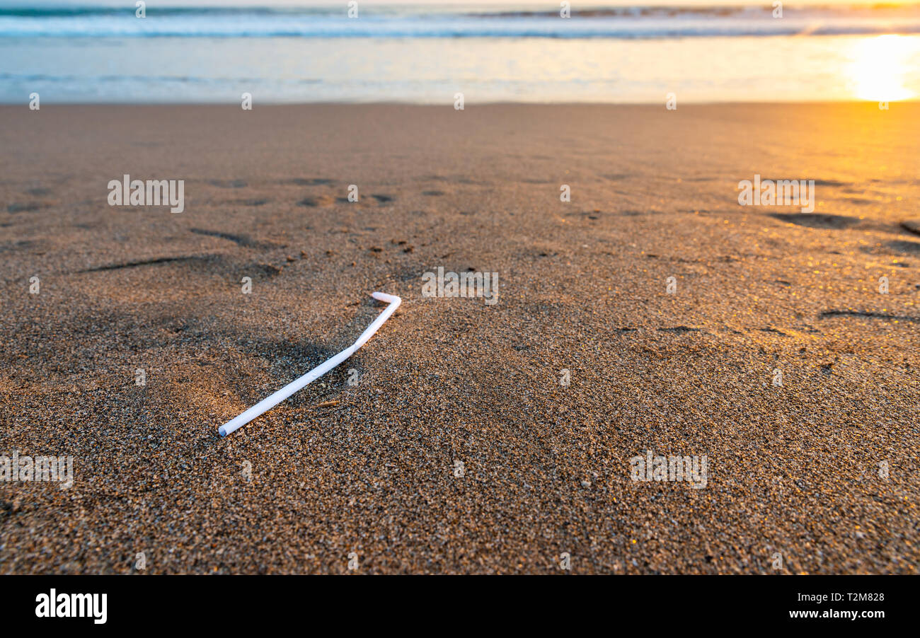 A single plastic straw on a beach at sunset, plastic pollution concept ...