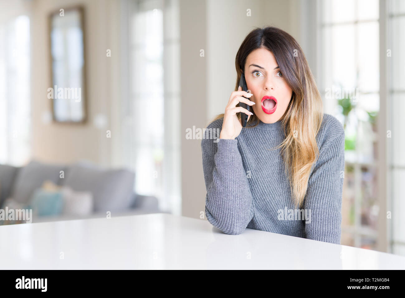 Young beautiful woman talking on the phone at home scared in shock with ...