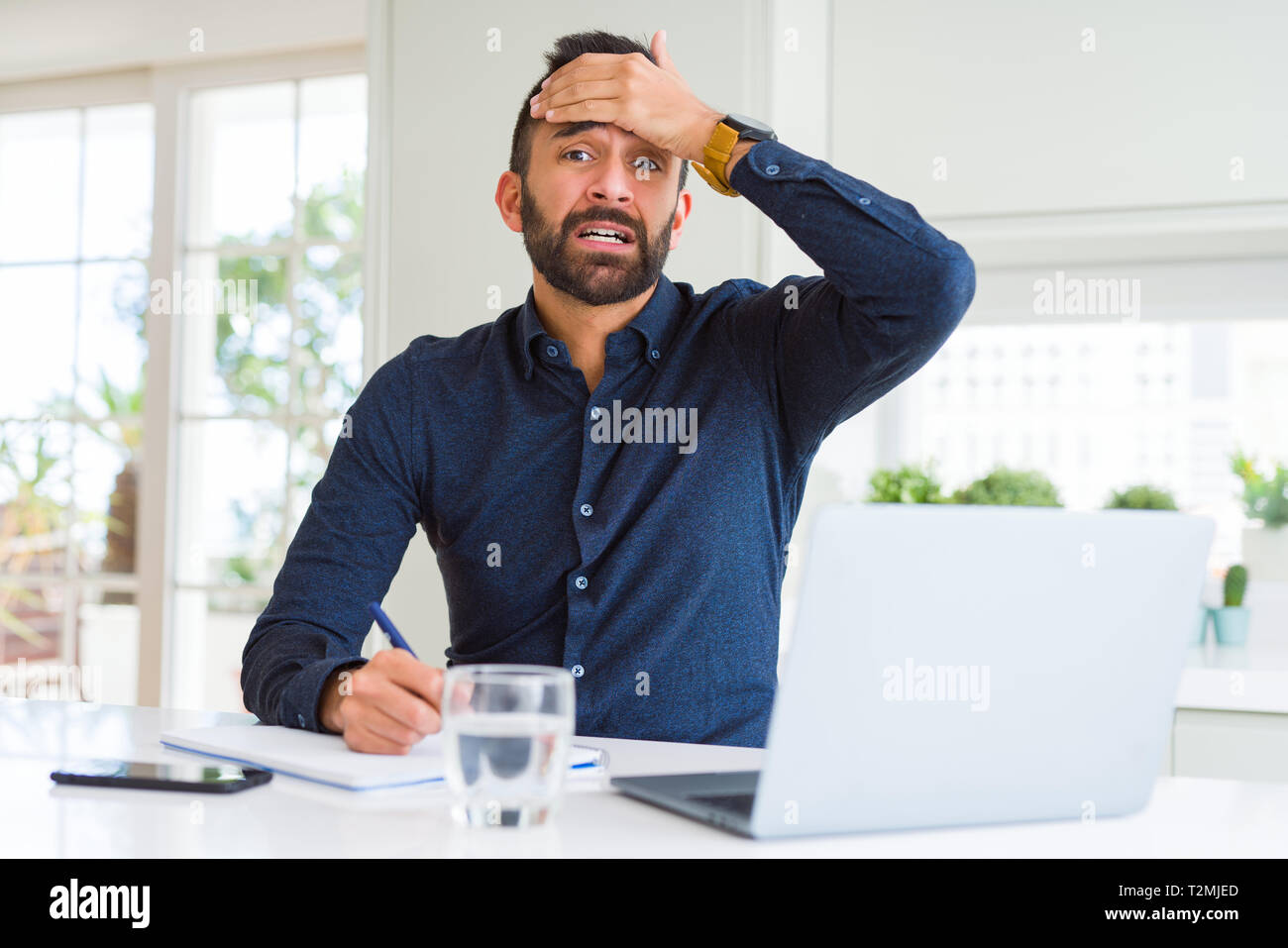 Handsome hispanic man working using computer and writing on a paper ...