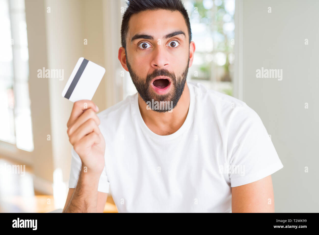 Handsome hispanic man holding credit card scared in shock with a ...