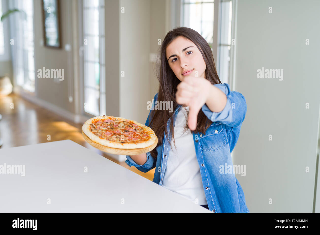 Beautiful young woman eating homemade tasty pizza at the kitchen with ...
