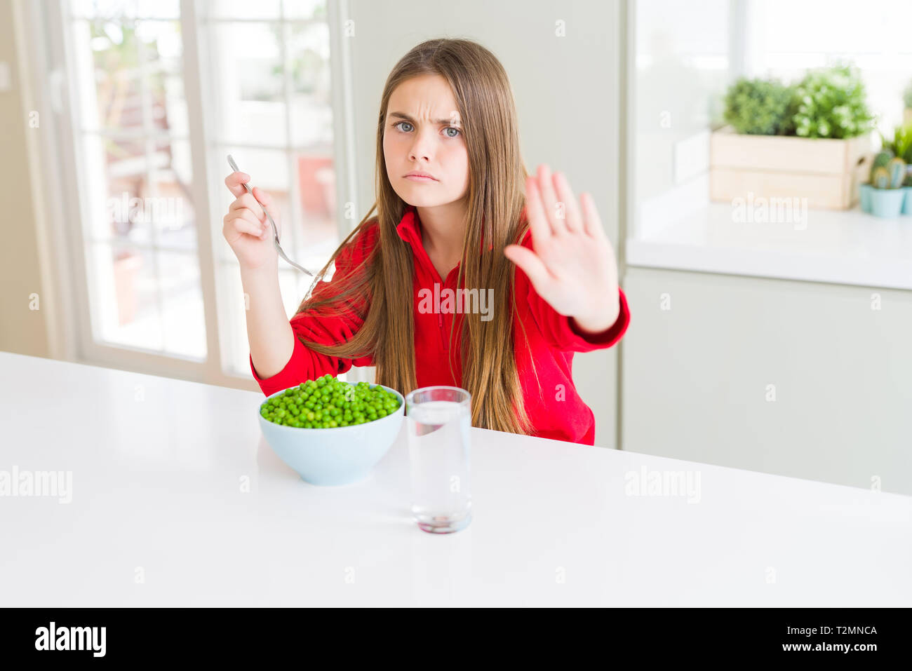 Beautiful young girl eating healthy green peas with open hand doing ...