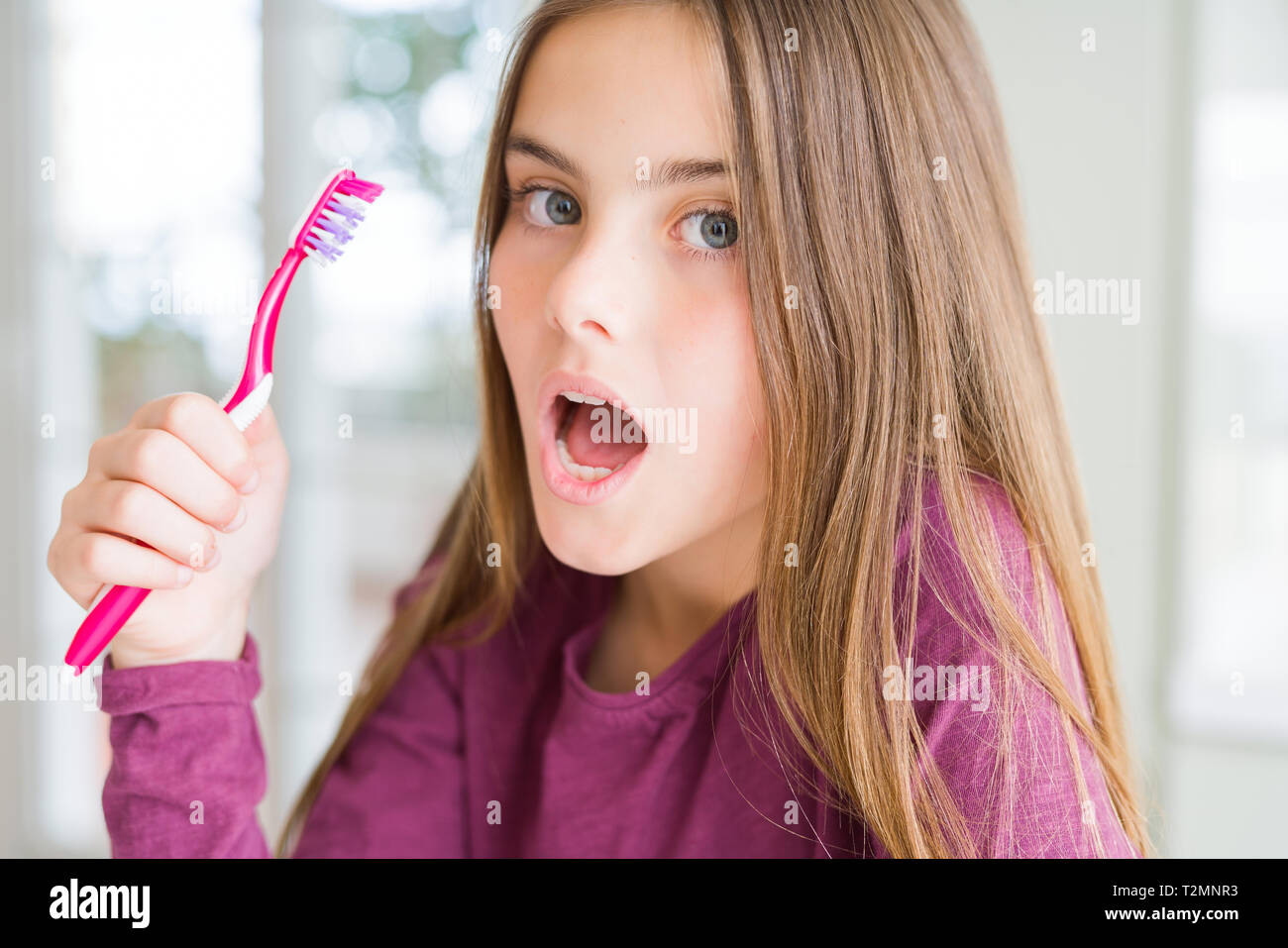 Beautiful young girl kid holding pink dental toothbrush scared in shock ...