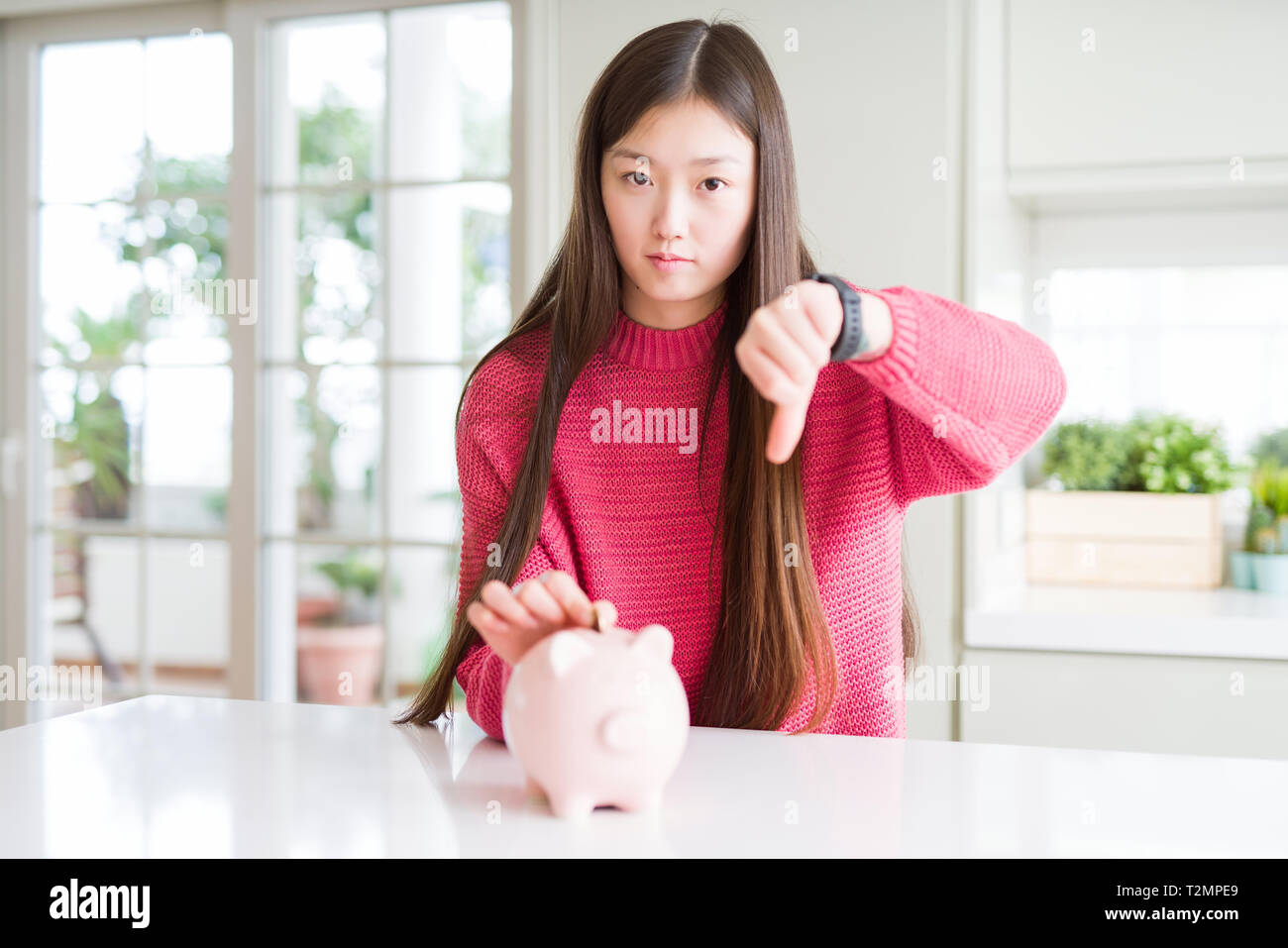 Beautiful Asian woman putting a coin inside piggy bag with angry face ...