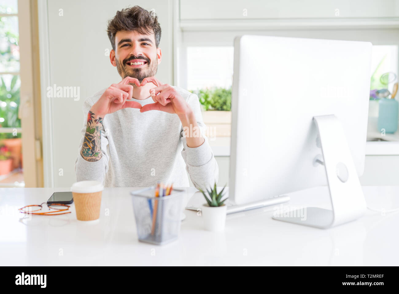 Young man working using computer smiling in love showing heart symbol ...
