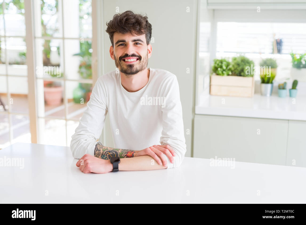 Handsome young man smiling cheerful at the camera with crossed arms and ...
