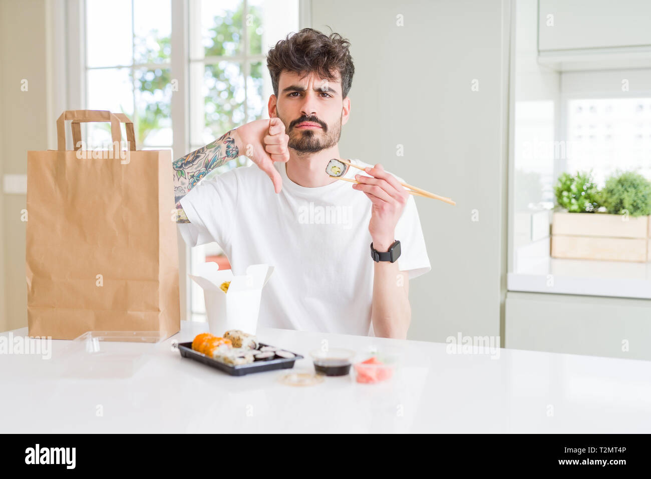 Young man eating asian sushi from home delivery with angry face ...