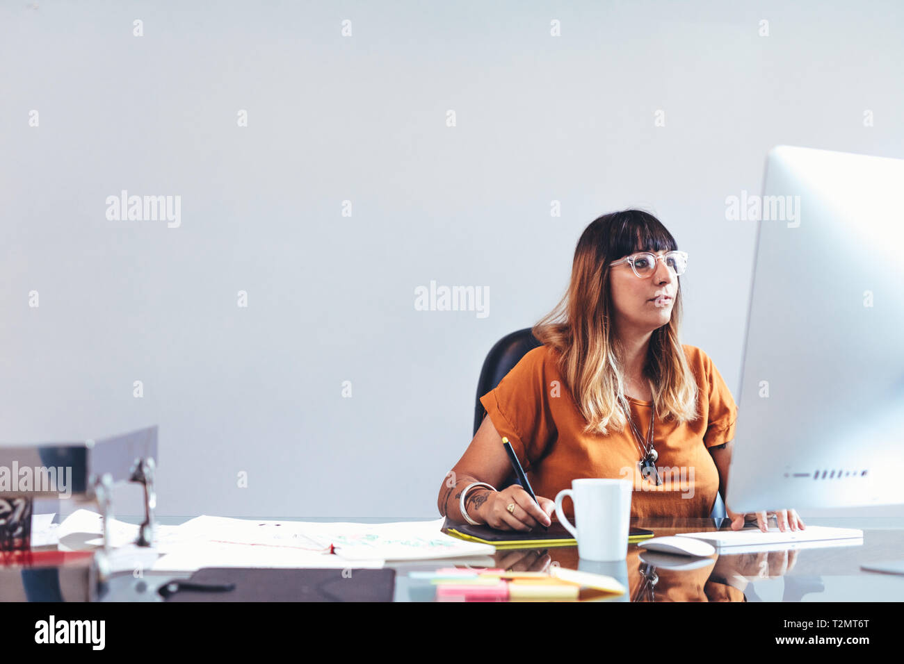 Illustrator sitting at her desk in office making a drawing using a ...