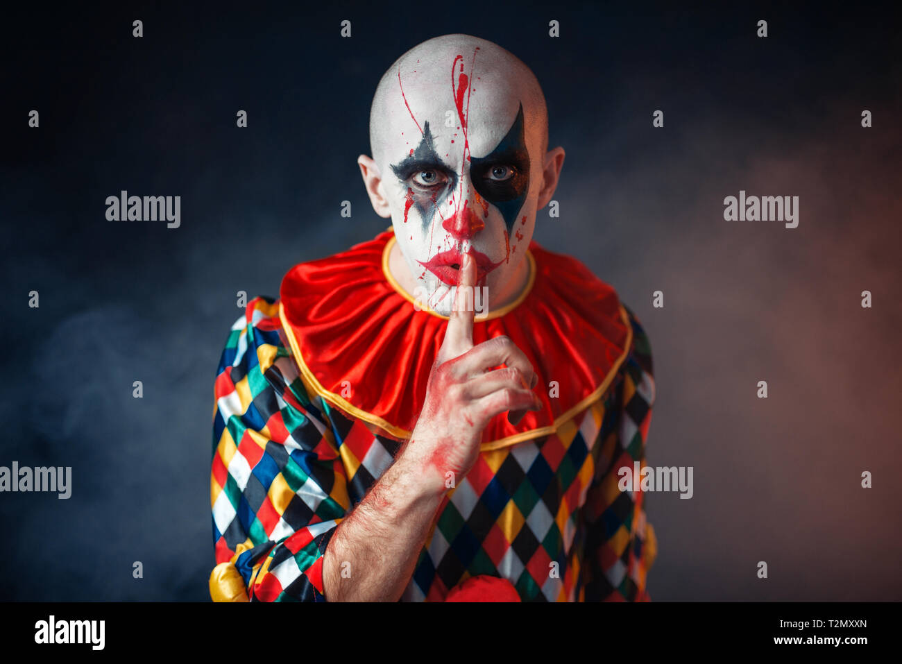 Portrait of mad bloody clown shows the quiet sign, face in blood. Man ...