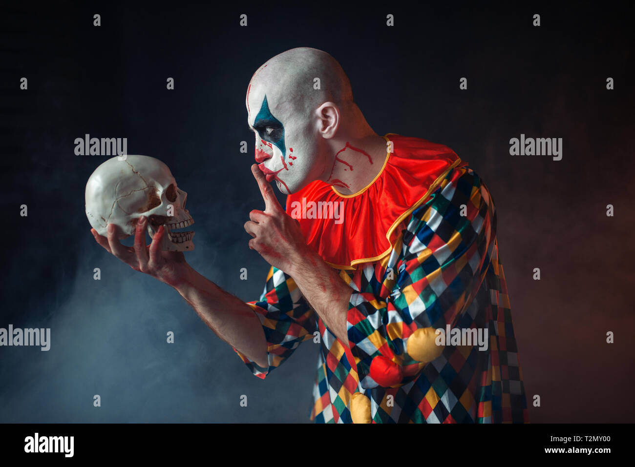 Portrait of mad bloody clown shows the quiet sign to the skull, face in ...