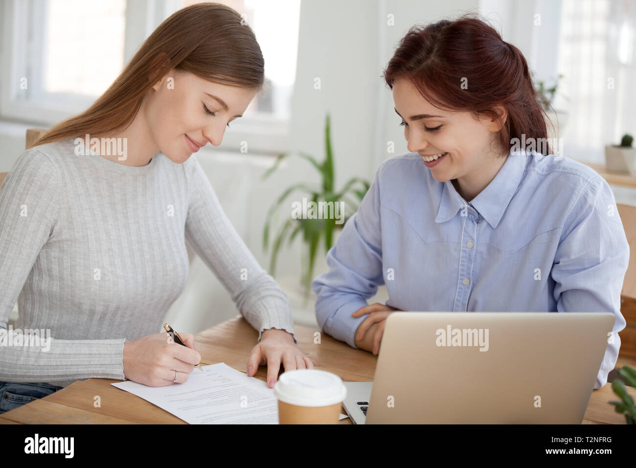 Two positive happy millennial young business women sitting at the desk ...