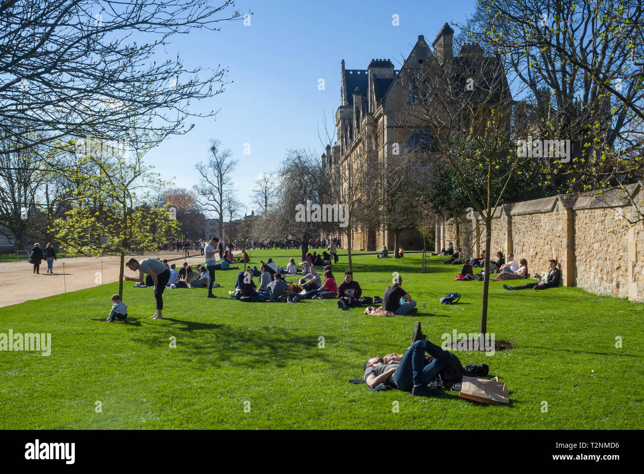 Tourists and students relax in the Spring sunshine on the grass by the ...