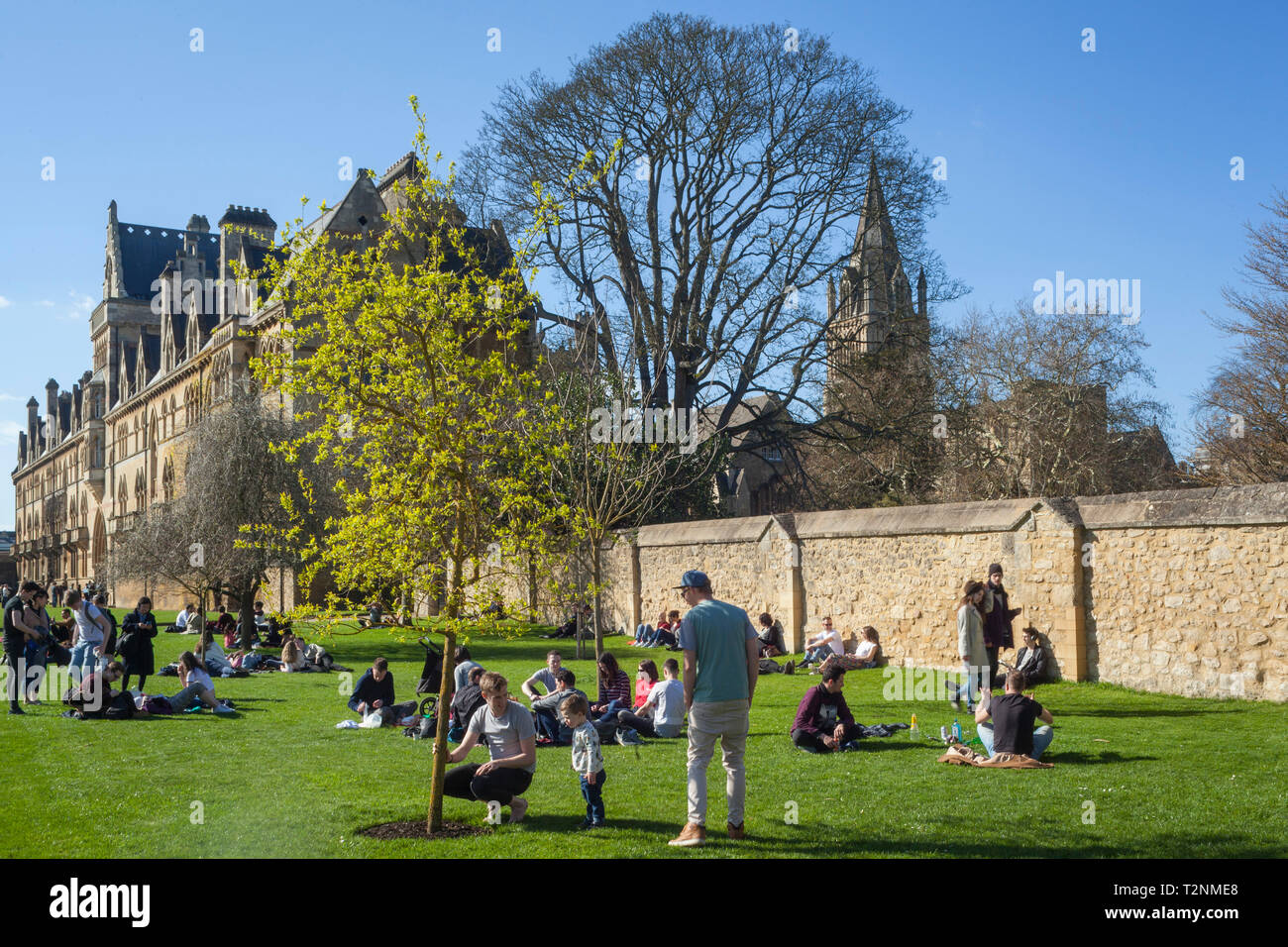 Tourists and students relax in the Spring sunshine on the grass by the ...