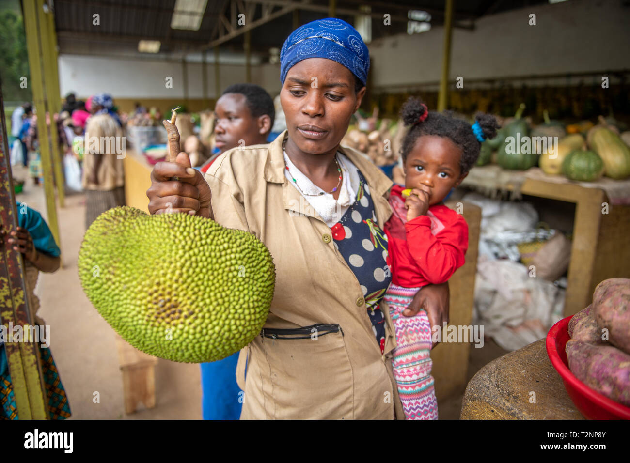 A woman holds her child under her arm while examining a jackfruit at ...