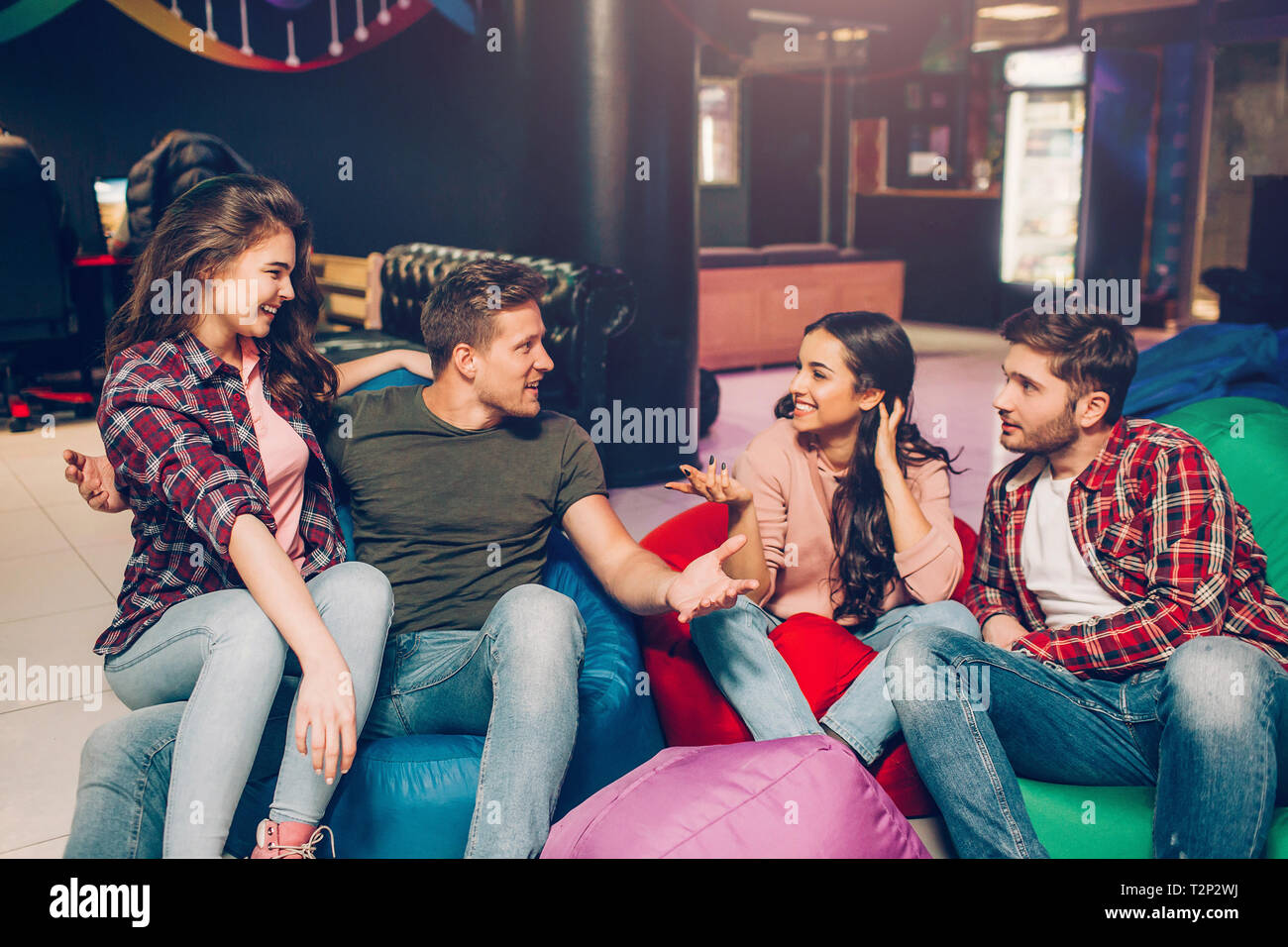 Four people sitting on inflatable bags in playing room and talk to each ...