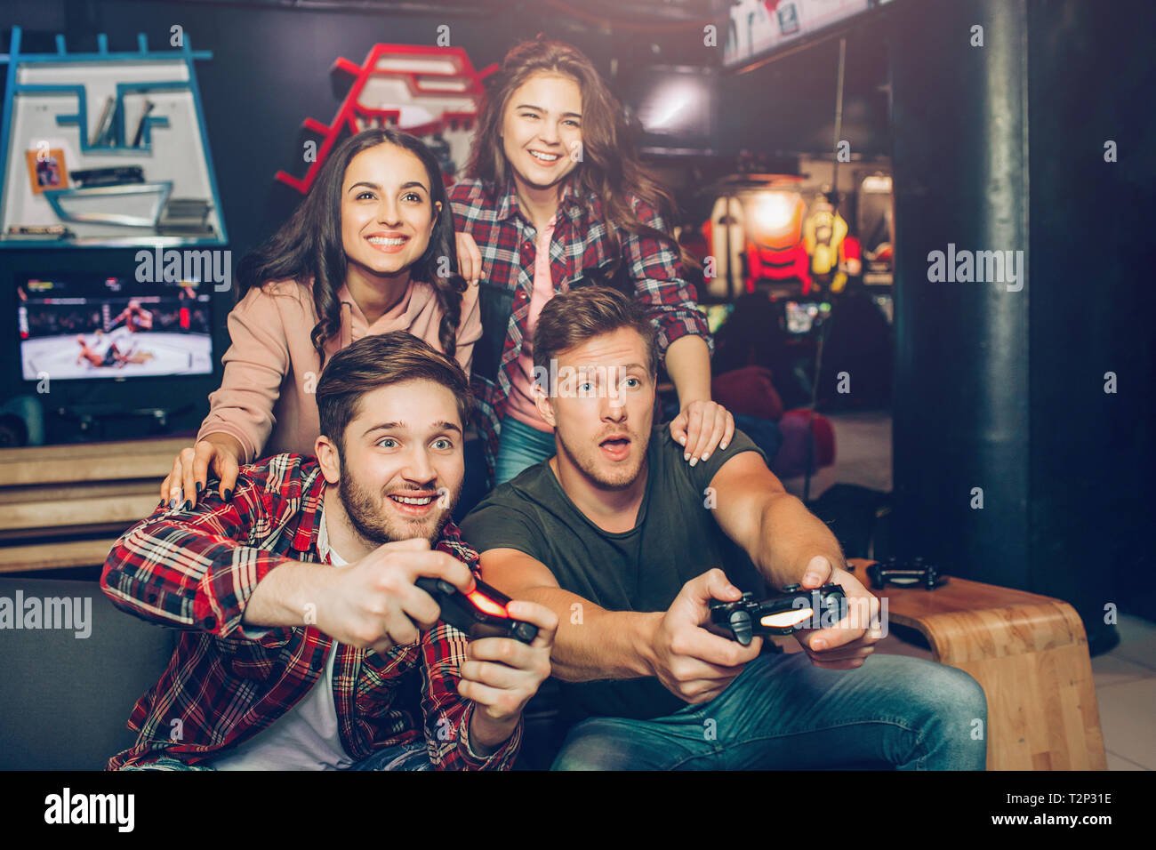 Excited young men sit on sofa in playing room. They hold joysticks and ...