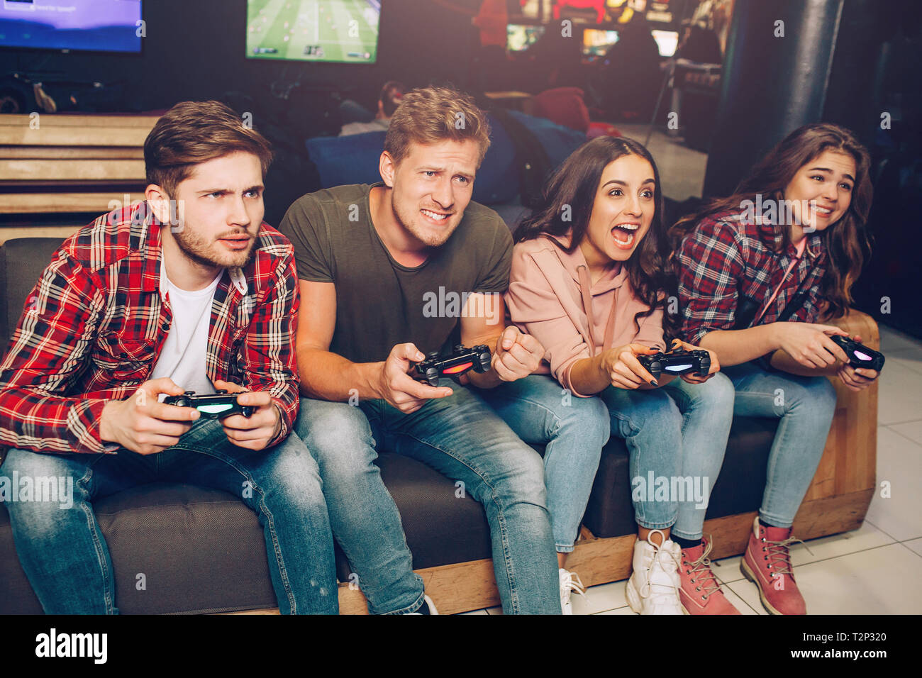 Picture of four people sitting in one raw on sofa in playing room. They ...