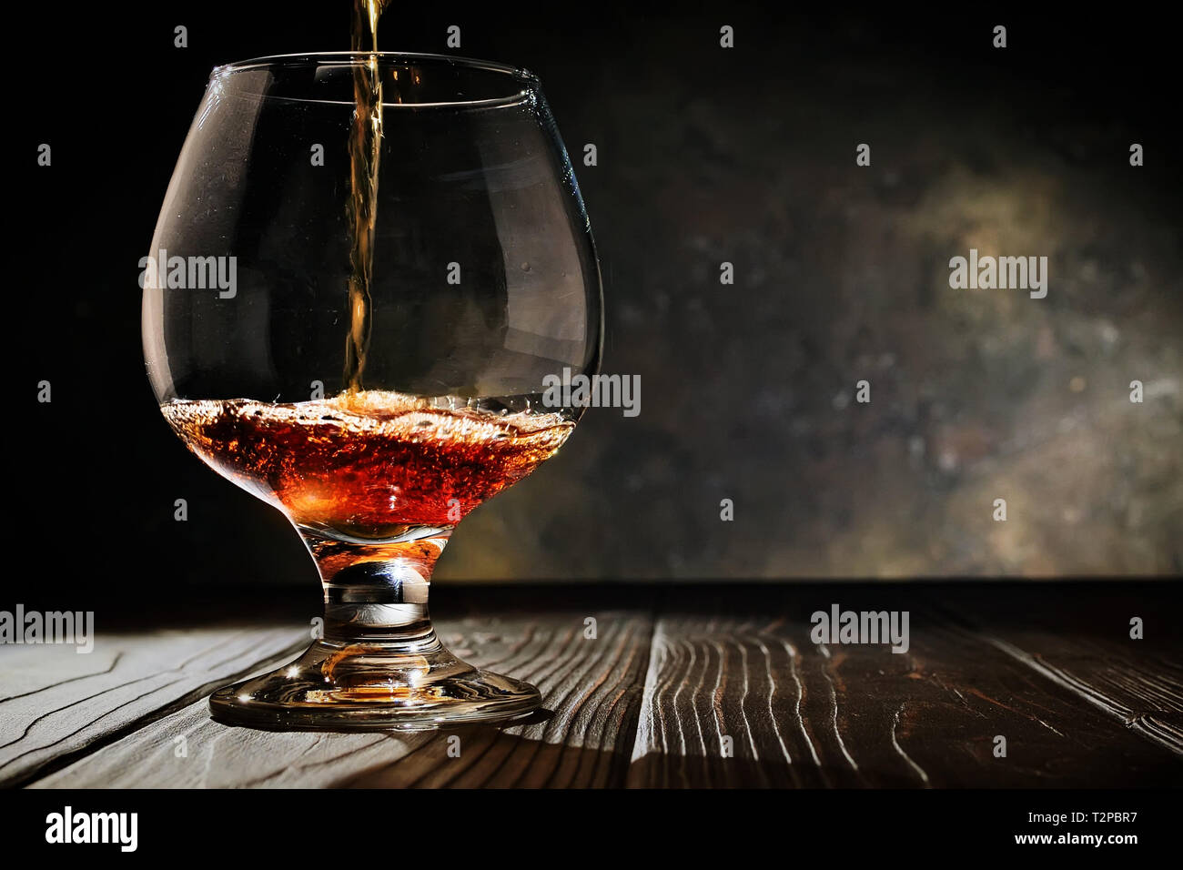 Cognac is poured into a glass on an old dark wooden background. Free ...