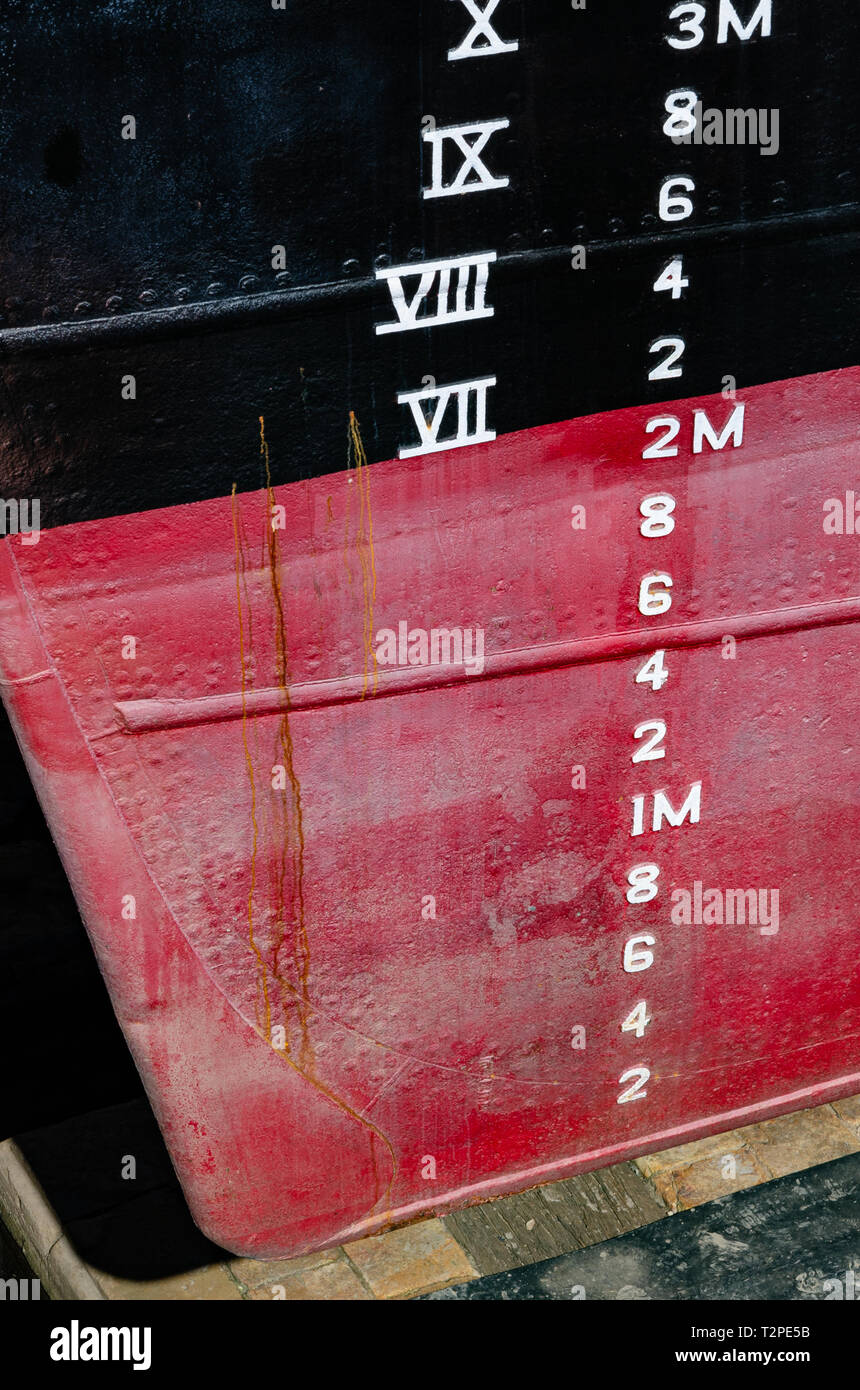 An iron ship hull painted red and black with white depth markers Stock ...
