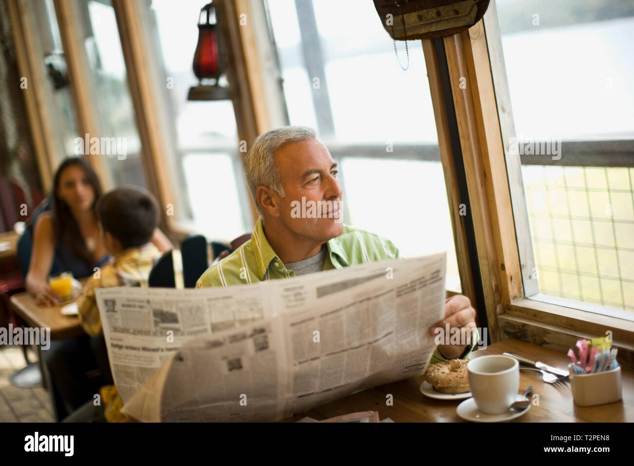 Mature man looking out a window while holding a newspaper inside a cafe ...