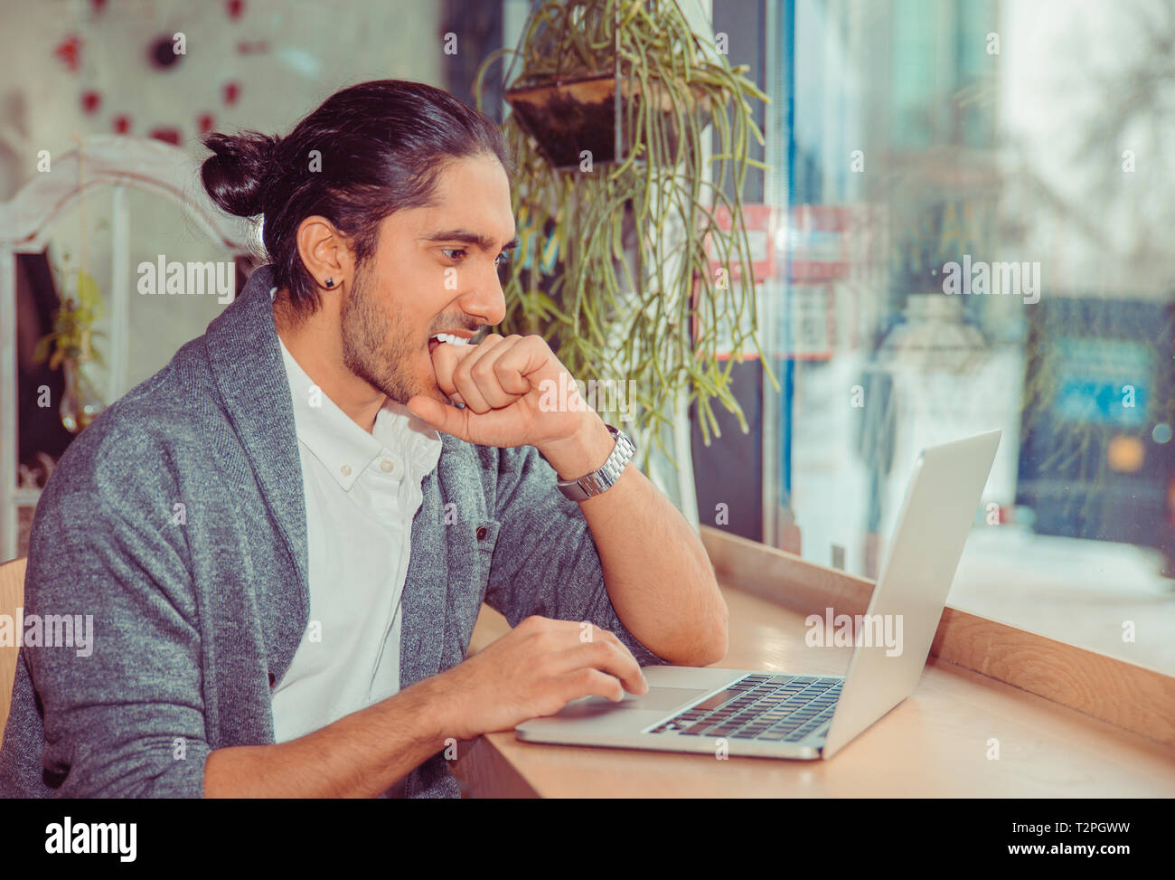 Nervous man in side profile biting fist while watching news on laptop ...