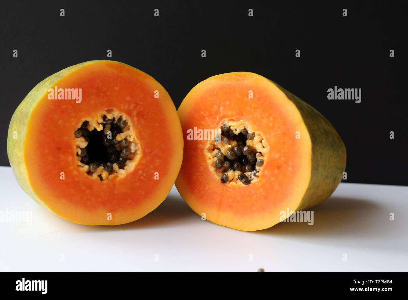 Two papaya halves on white cutting board against dark background Stock ...