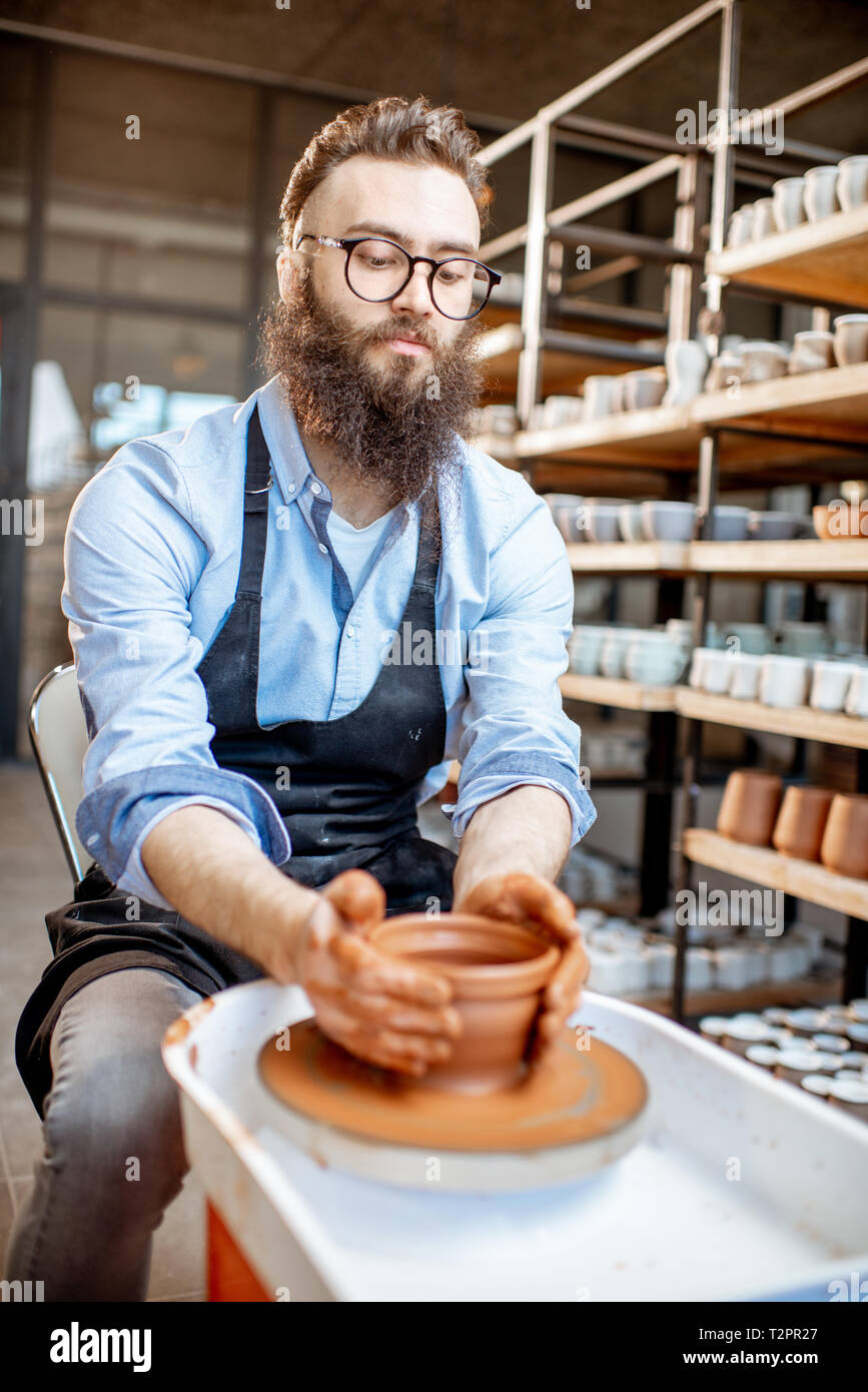 Handsome man as a potter worker in apron making clay jugs on the ...