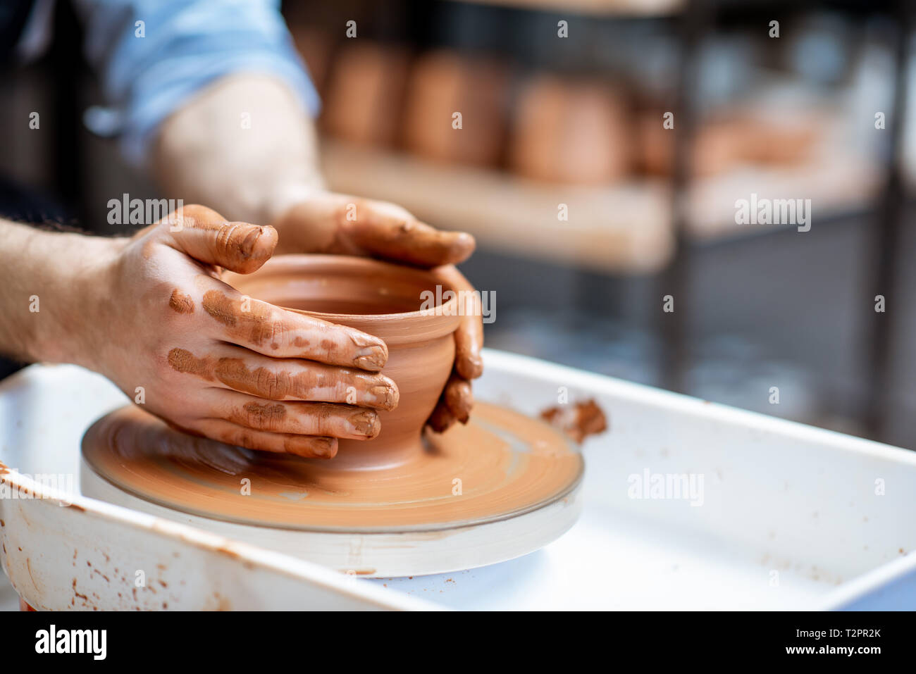Man making clay jug forming shape by hands on the pottery wheel indoors ...