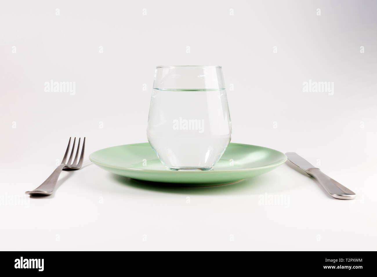 glass of water in a plate with knife and fork isolated on white ...