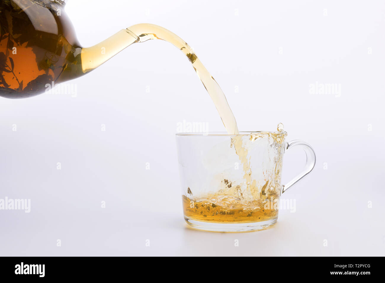 Glass teapot pouring herbal tea into cup isolated on white background ...