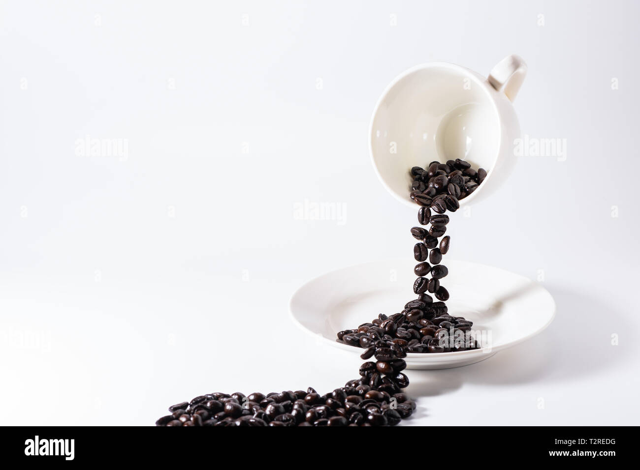 Coffee beans poured from coffee cup on saucer then spilled on white ...