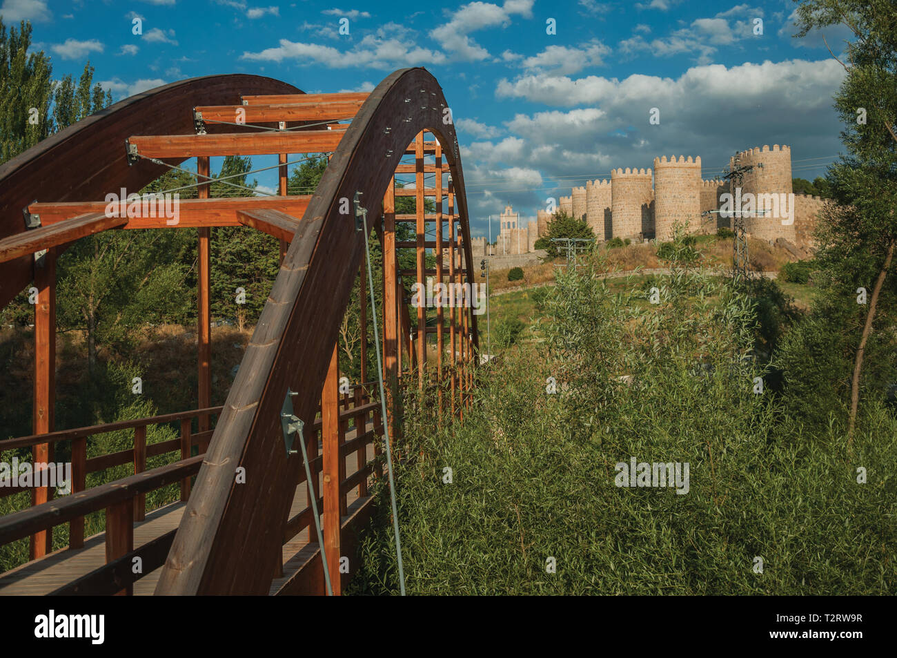 Wooden bridge over the Adaja River with trees and the city of Avila at ...