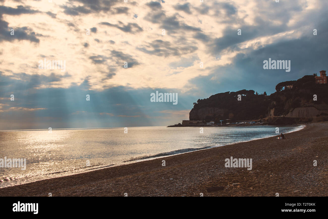 sunset on the beach, rays of the sun penetrate the blanket of clouds ...