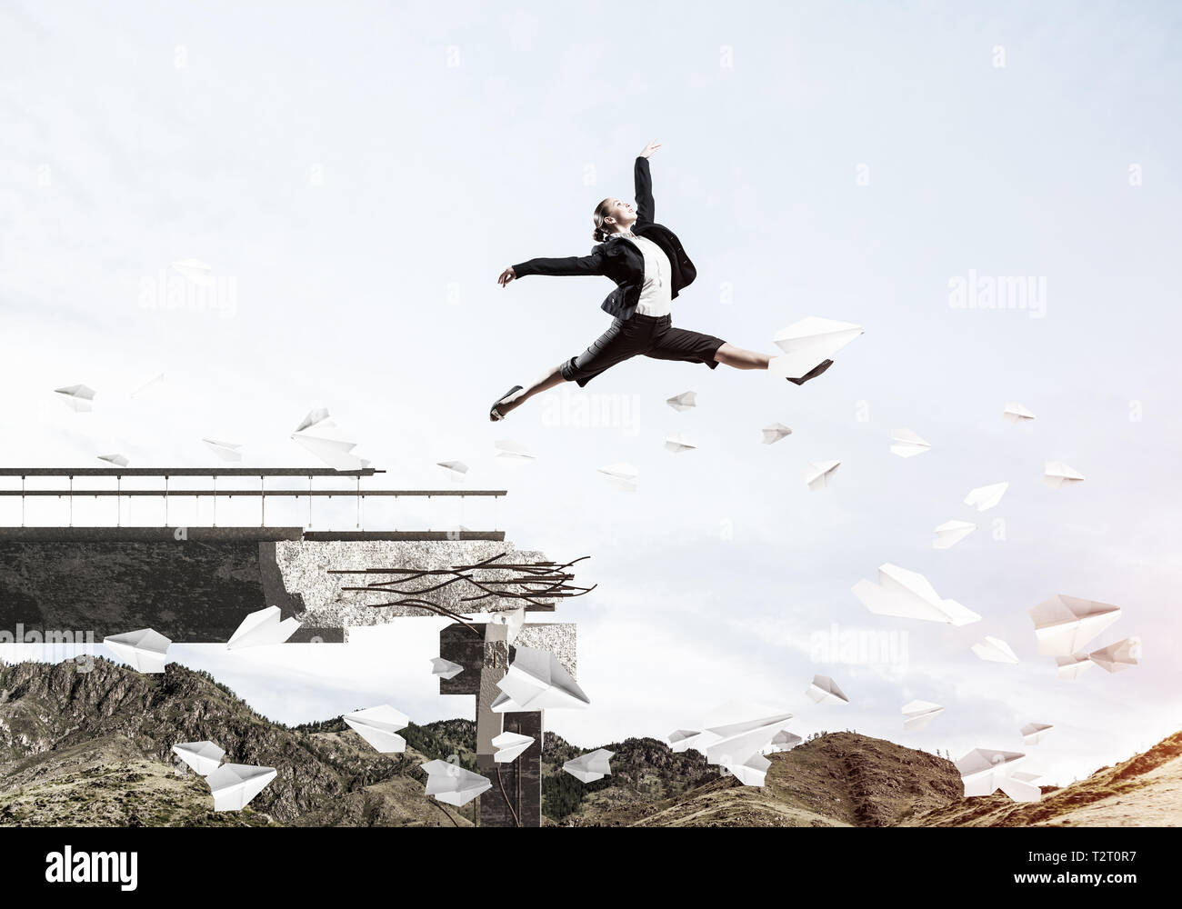Business woman jumping over gap in bridge among flying paper planes as ...