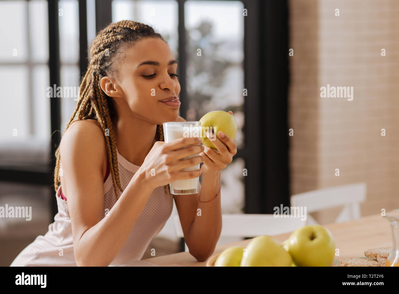 Apple and milk. Woman with nice braids enjoying apple and glass of milk ...