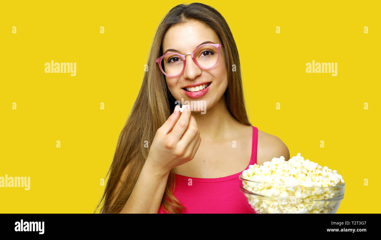 Happy cheerful woman eating pop corn on yellow background. Girl holding ...