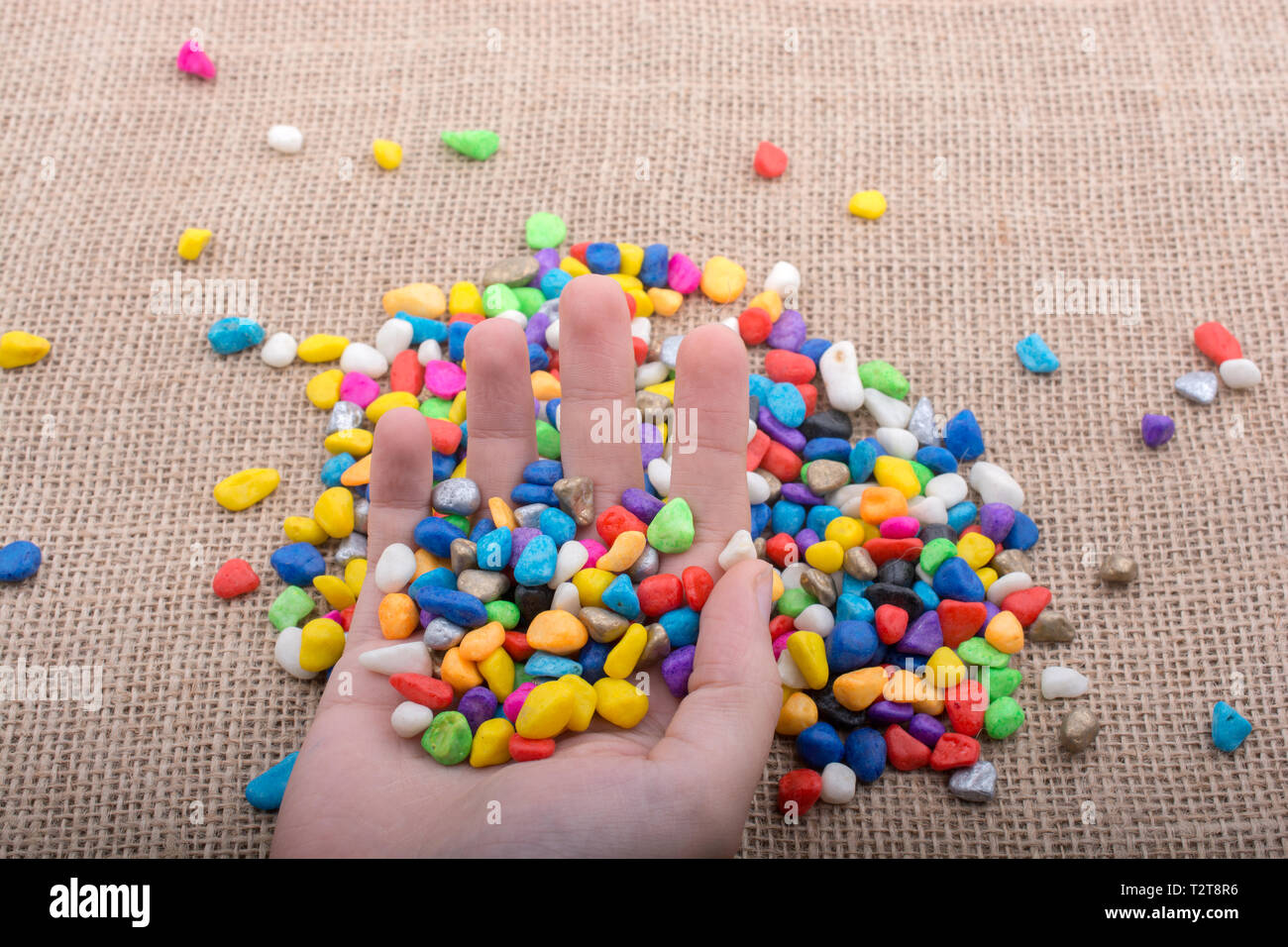 Colorful little pebbles in hand and on canvas ground Stock Photo - Alamy