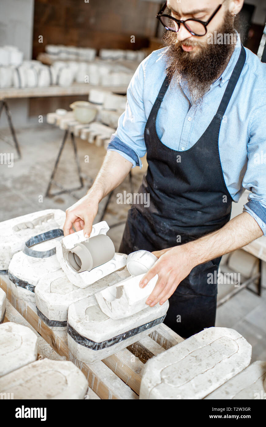 Handsome worker in apron getting clay products from the gypsum forms at ...