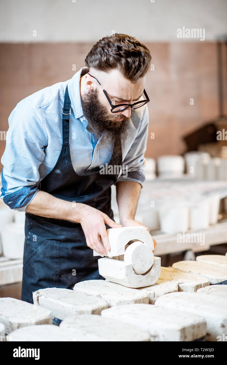Handsome worker in apron getting clay products from the gypsum forms at ...