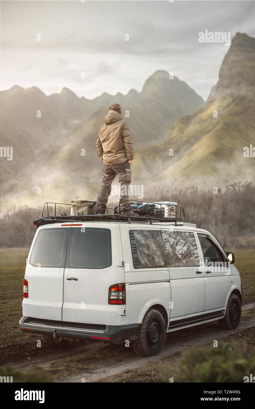Man standing on the roof of a van surrounded by mountains and nature ...