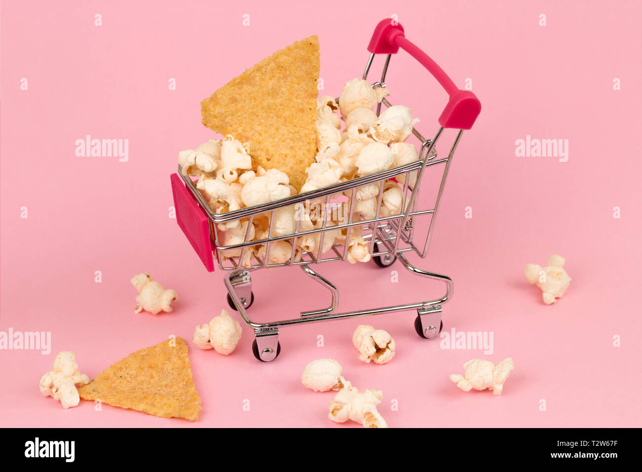 shopping cart full of popcorn and nachos on pink pastel background ...