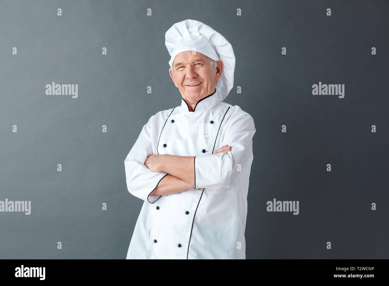 Senior male chef studio standing isolated on gray wall crossed arms ...