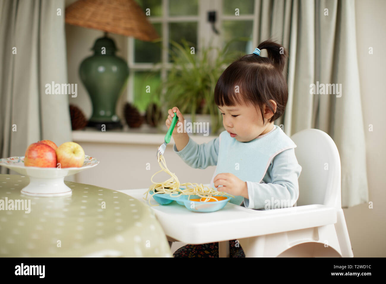 toddler girl eating healthy pasta and vegetable sitting on high chair ...