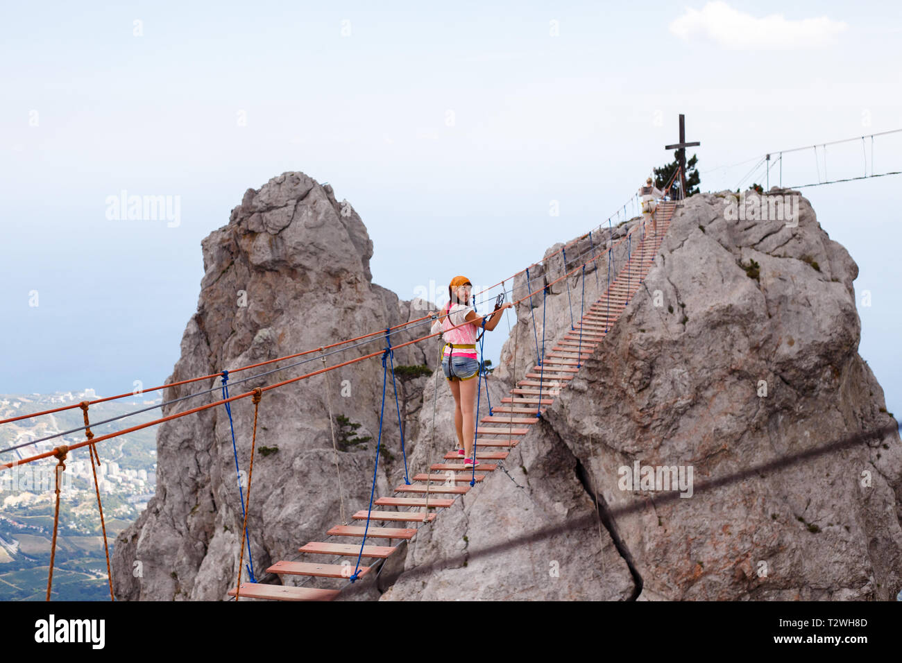 Photo of young woman walking up t rope ladder against cliff on summer ...
