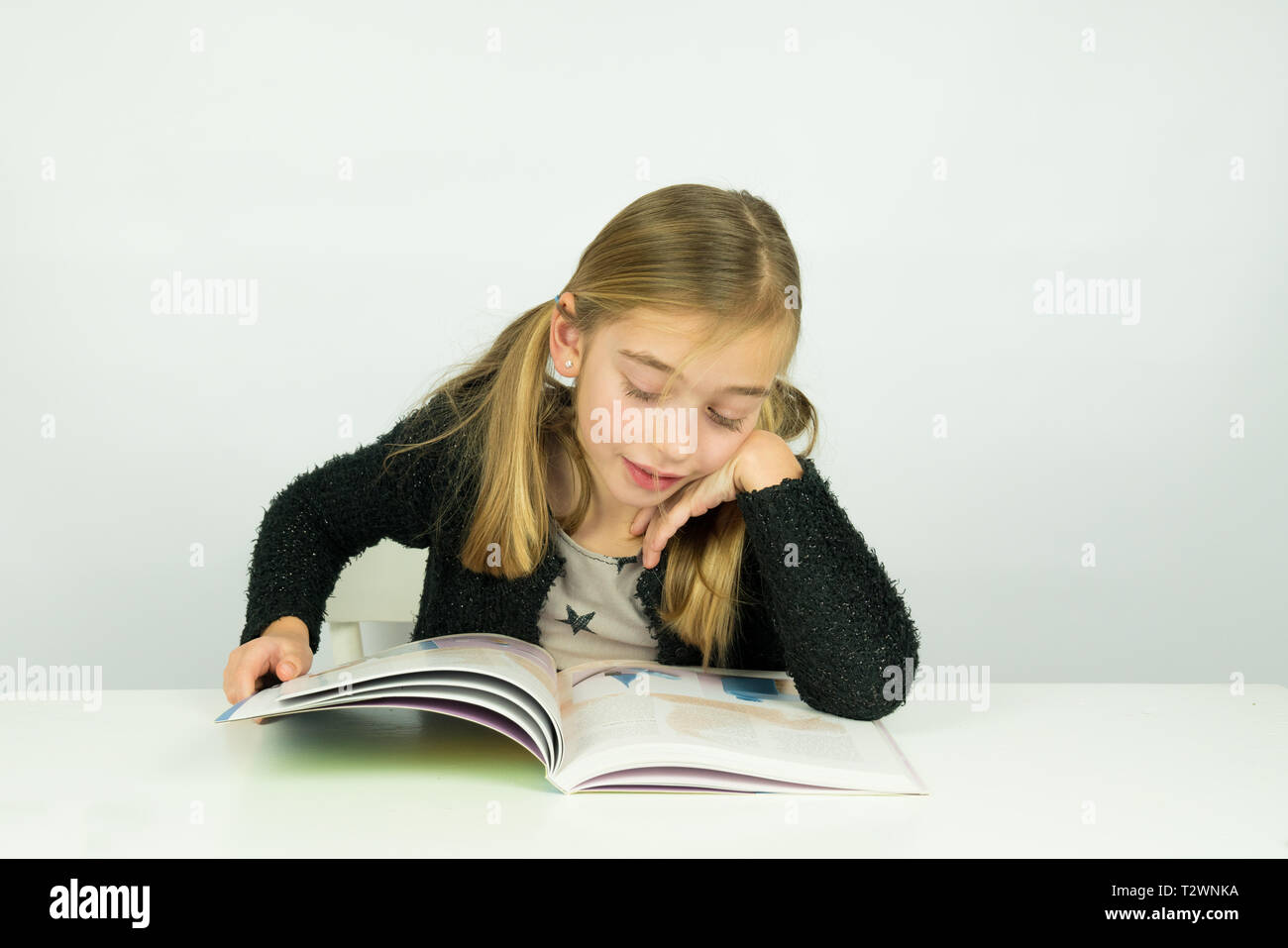 Portrait of a cute girl is reading a book, doing homework. She can do ...
