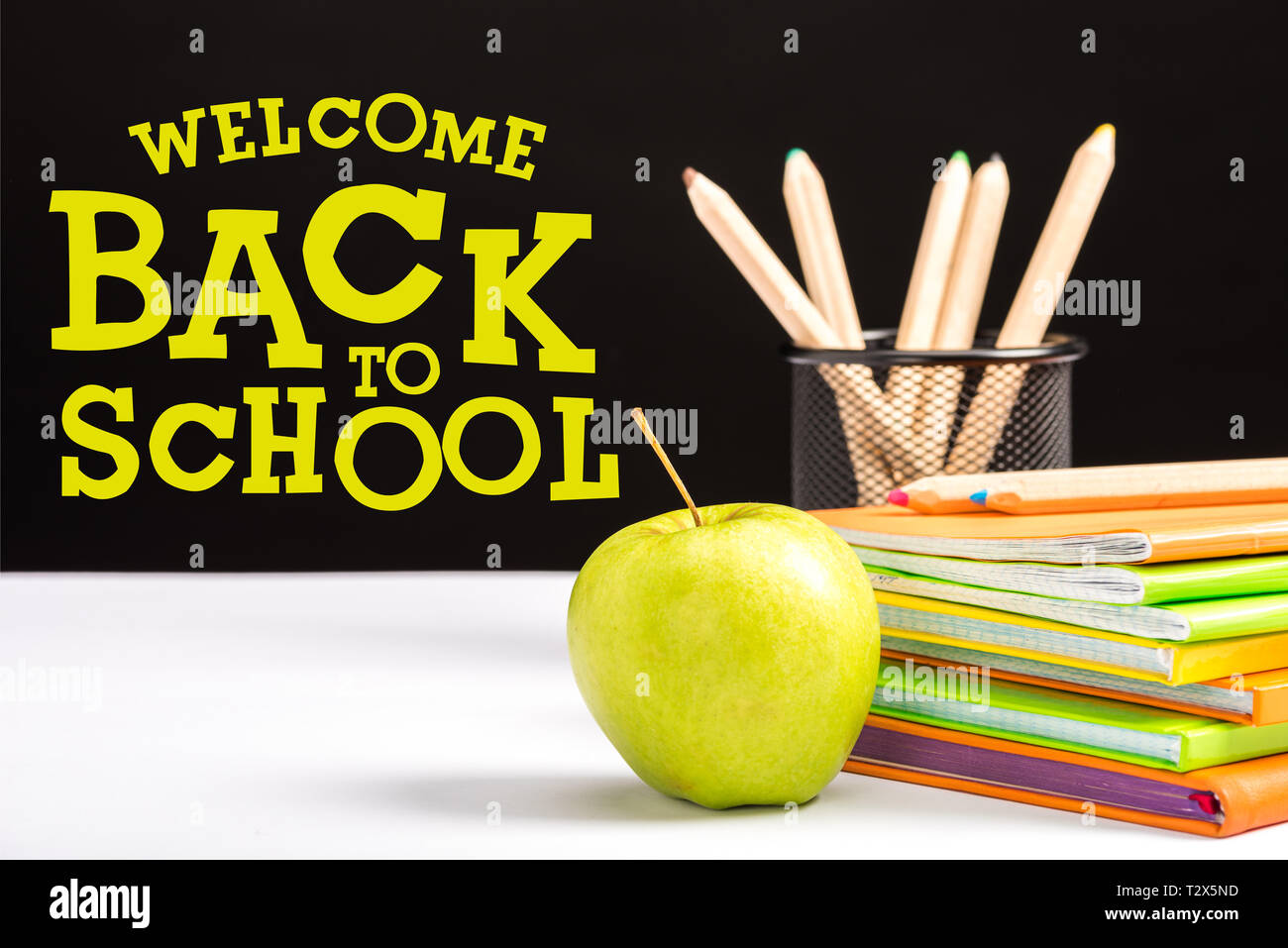 fresh apple, notebooks and color pencils on table with welcome back to ...