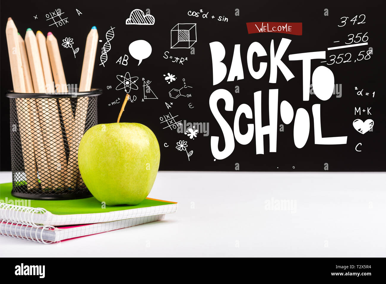 fresh apple, notebooks and color pencils on table with welcome back to ...