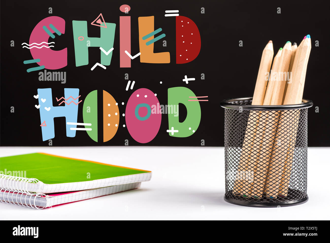 notebooks and color pencils on table with childhood lettering on black ...