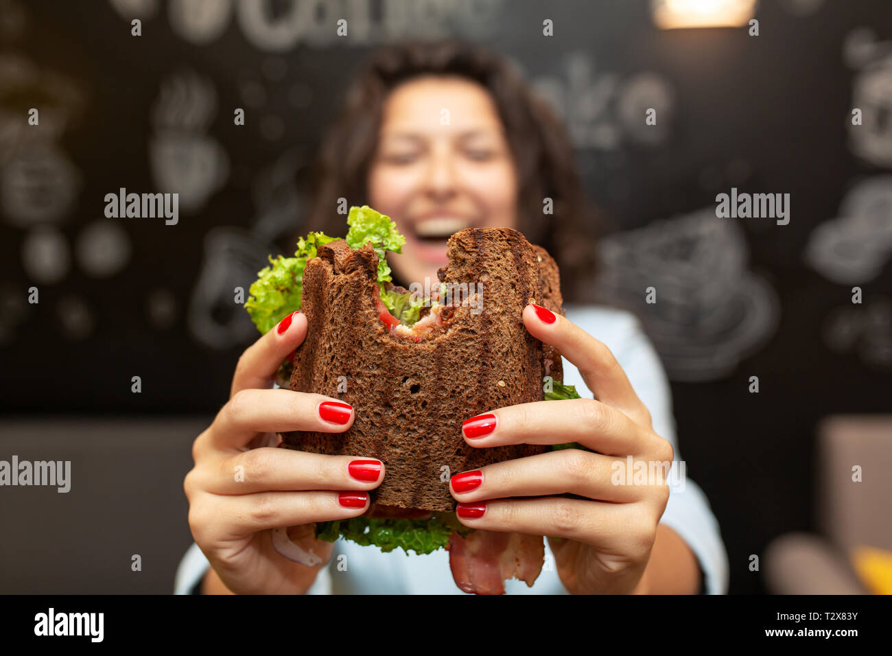Closeup funny blurred protrait of young woman hold bitten sandwich by ...
